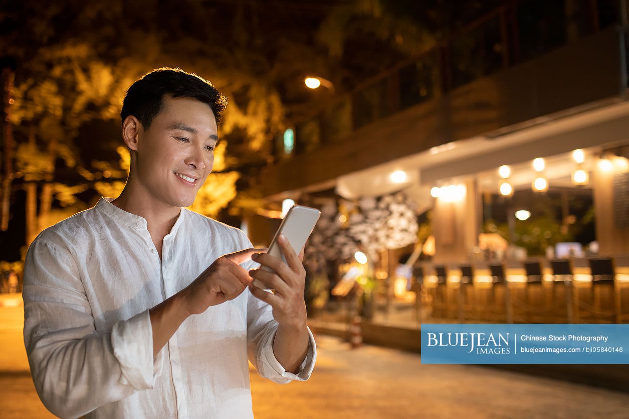 Happy young Chinese man using smartphone-High-res stock photo for download
