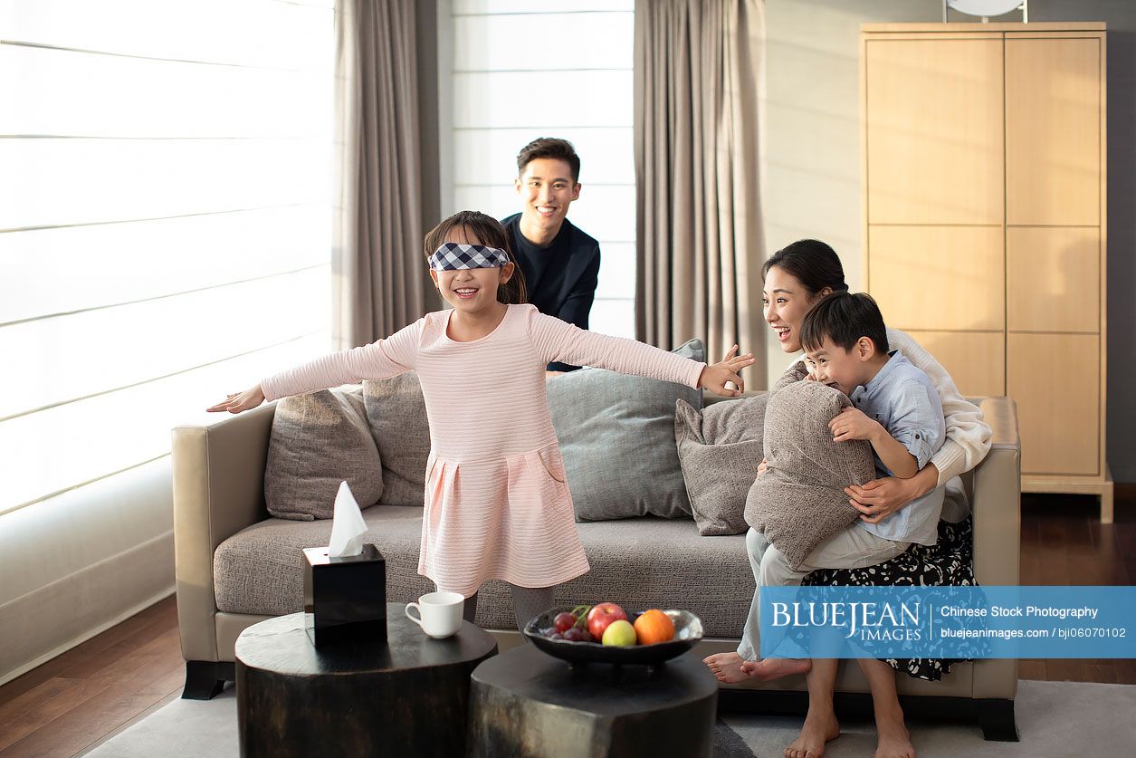 Happy young Chinese family playing hide and seek in living room-High ...