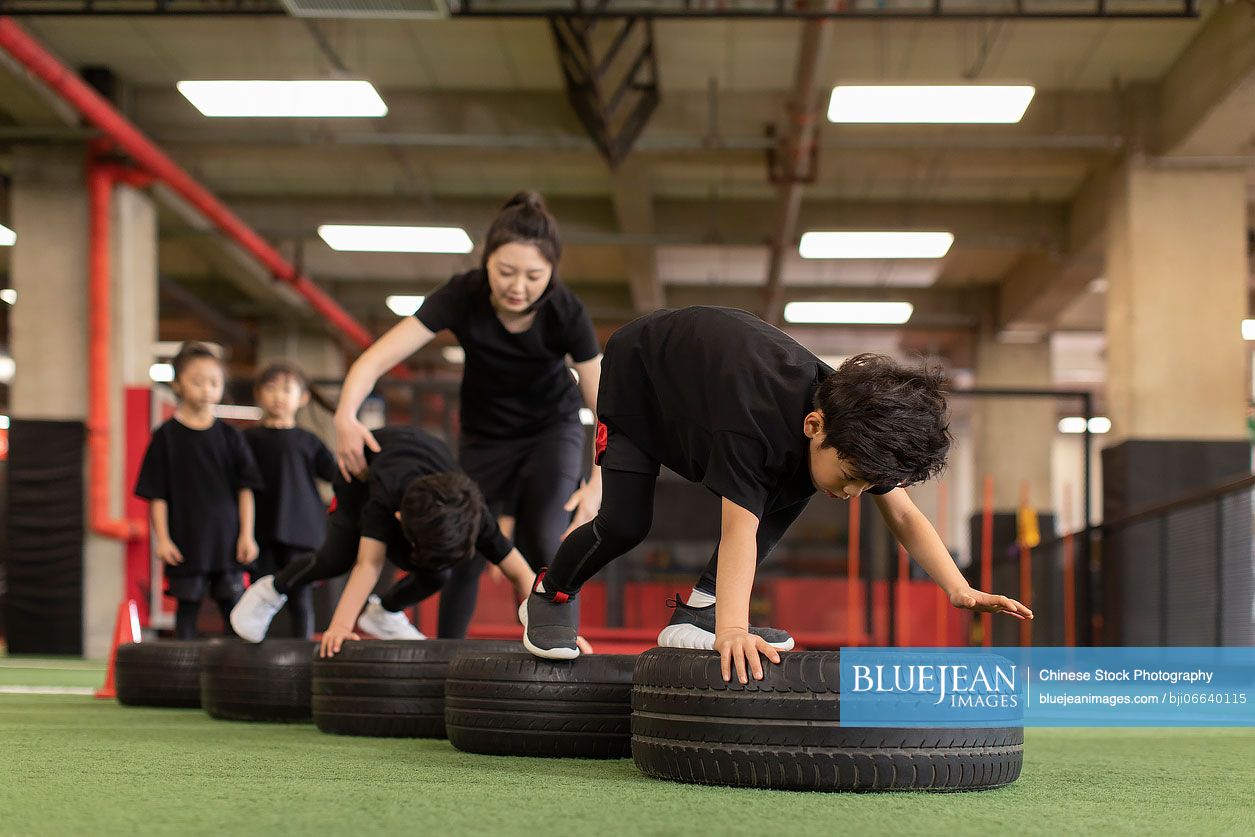 Active Chinese children having exercise class with their coach in gym ...