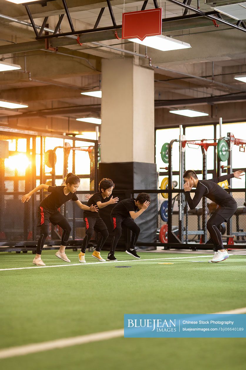 Active Chinese children having exercise class with their coach in gym ...