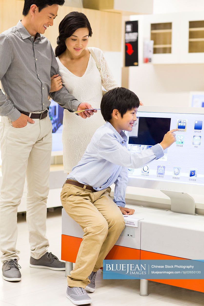 Cheerful Chinese boy touching the computer screen with parents beside ...