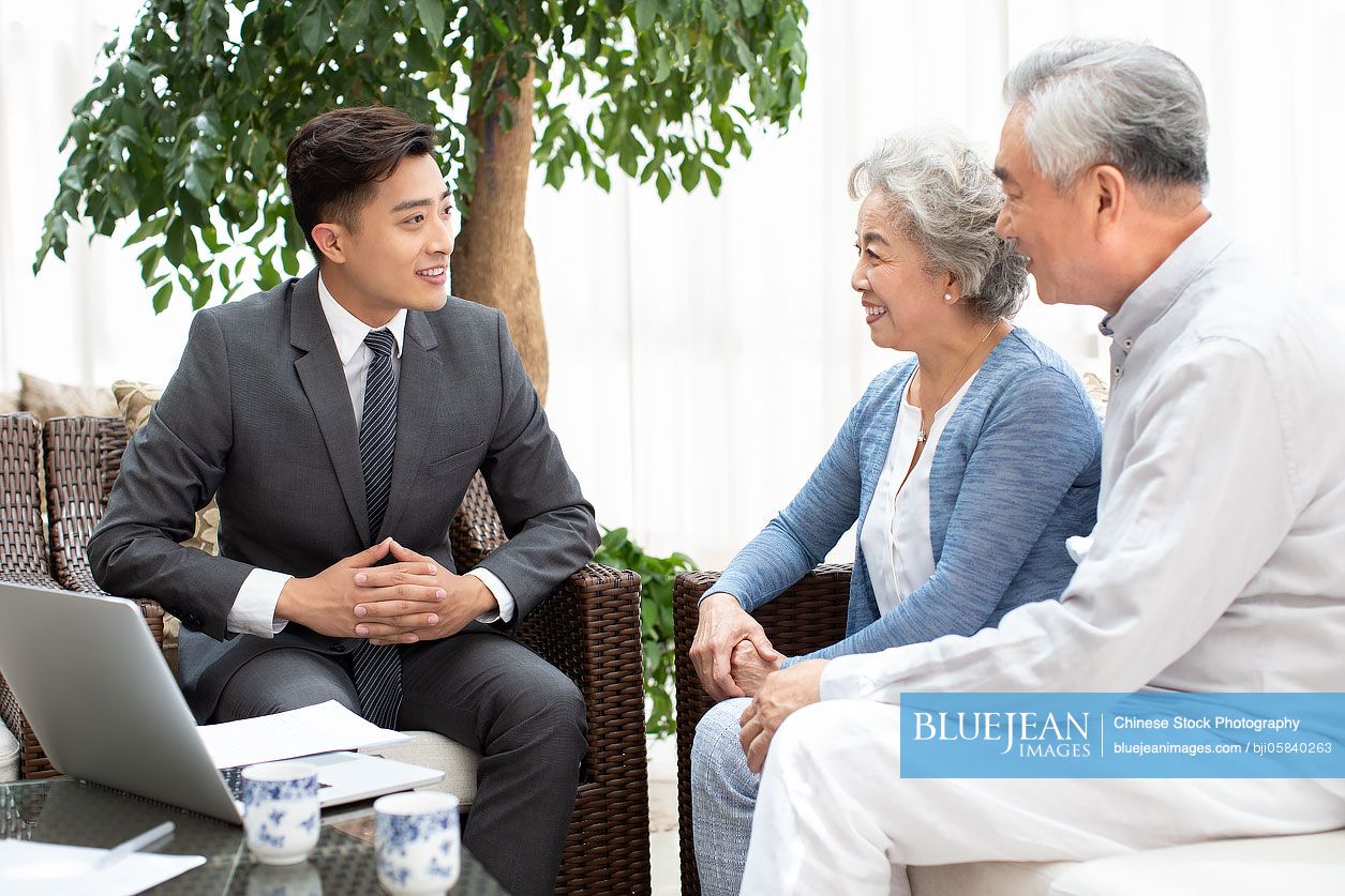 Happy senior Chinese couple talking with financial advisor in living ...
