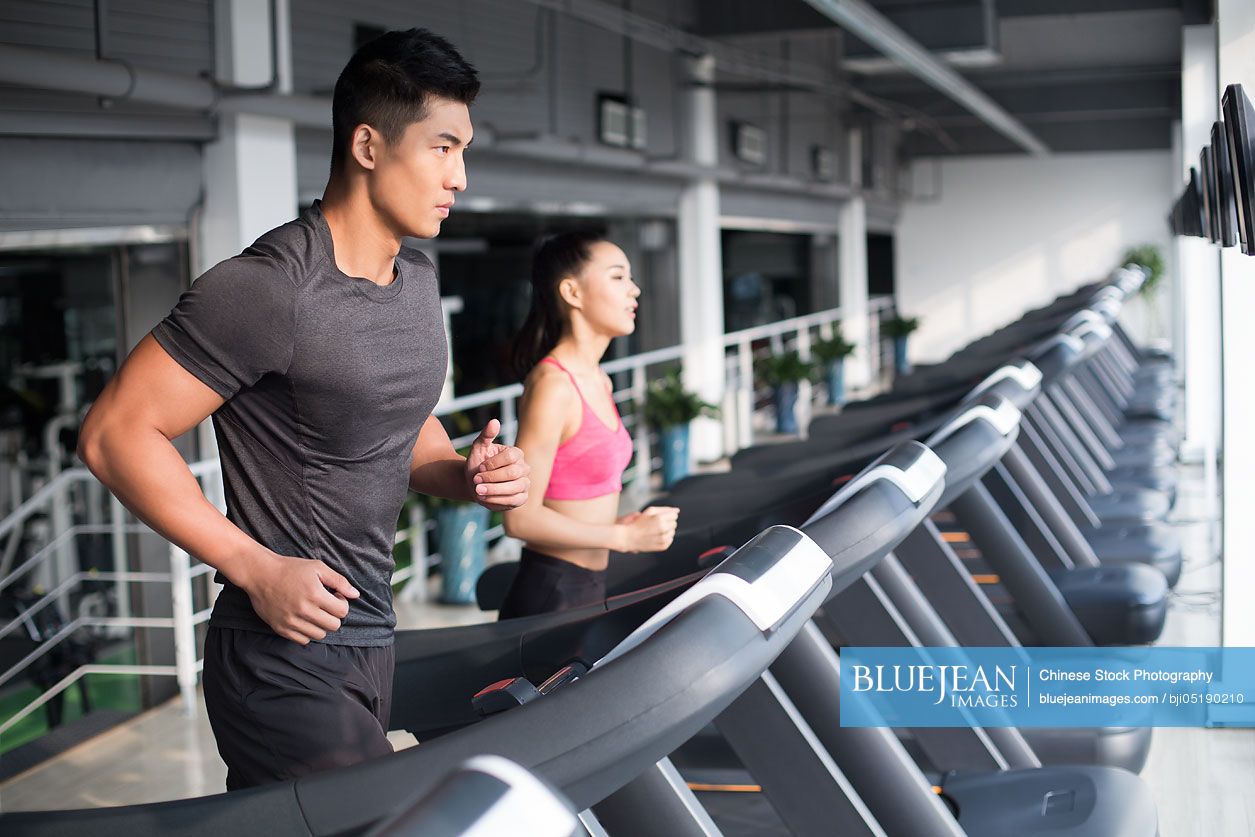 Young Chinese couple running on treadmills in gym-High-res stock photo for download