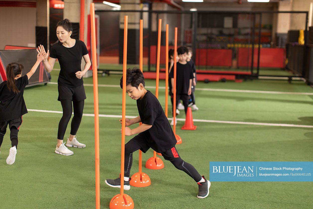 Active Chinese children having exercise class with their coach in gym ...