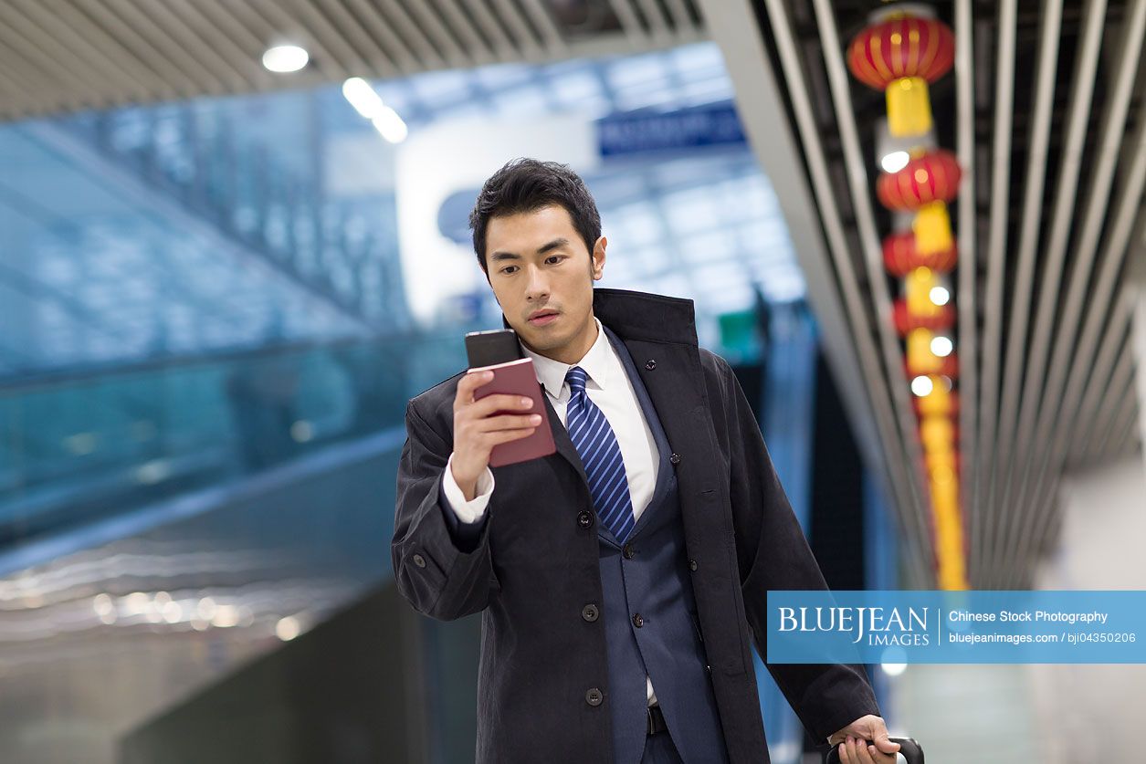 Young Chinese businessman walking in airport with passport and smart ...