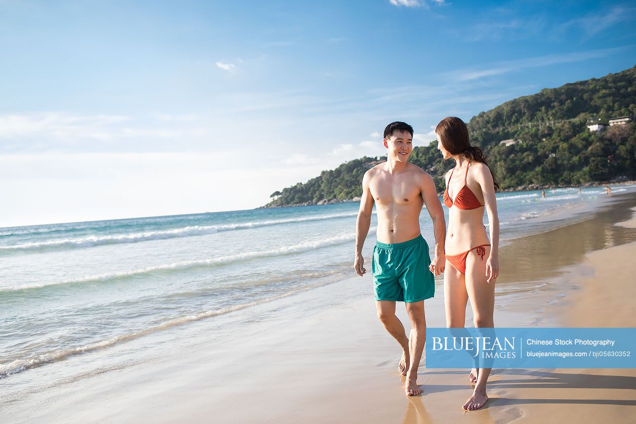 Happy young Chinese couple walking on beach-High-res stock photo for download