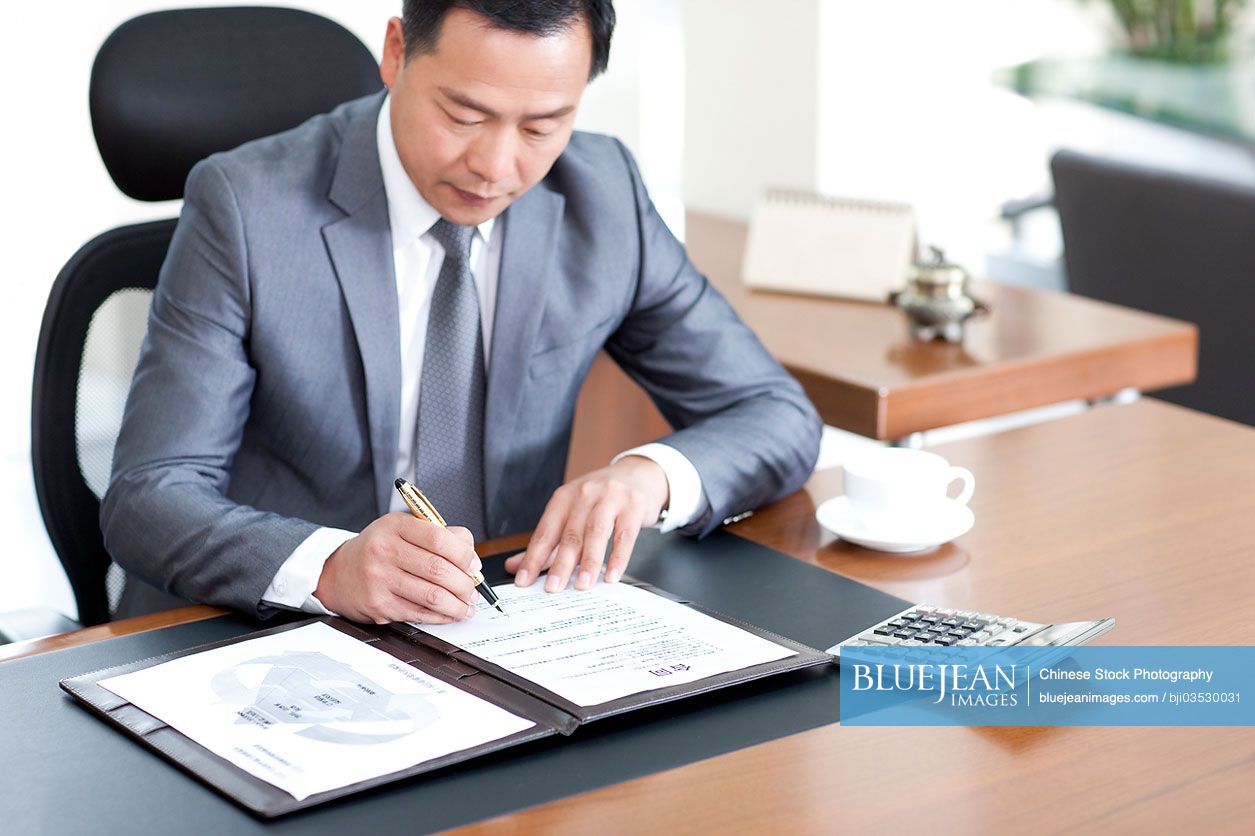 Mature Chinese businessman sitting at desk signing a document-High-res ...