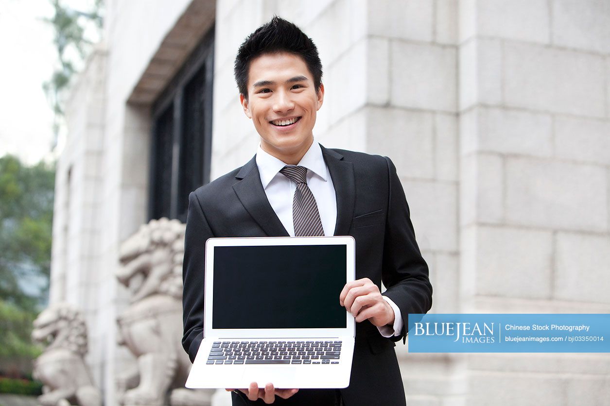 Happy young Chinese businessman with a laptop outside a building, Hong ...