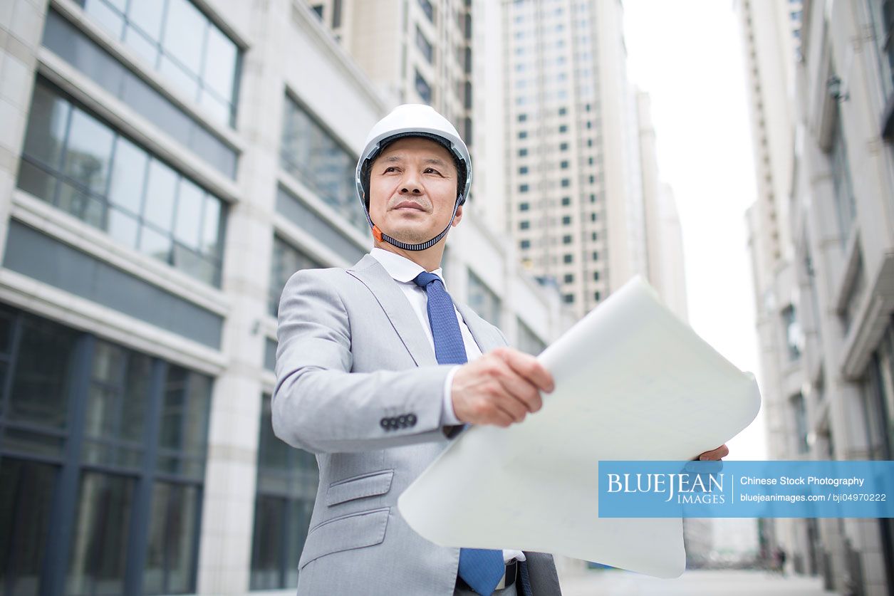 Chinese male architect looking at view with blueprint outdoors-High-res ...