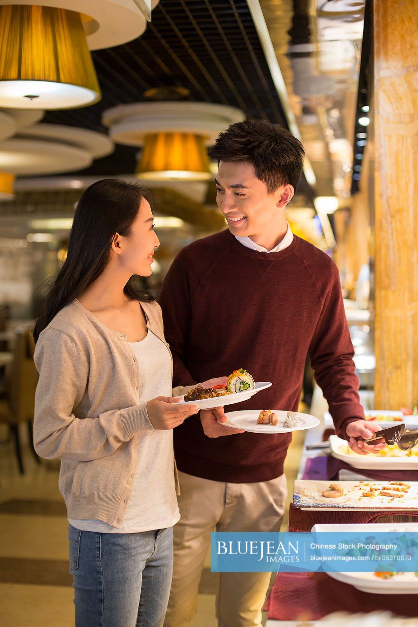 Cheerful young Chinese couple taking food from buffet table-High-res ...