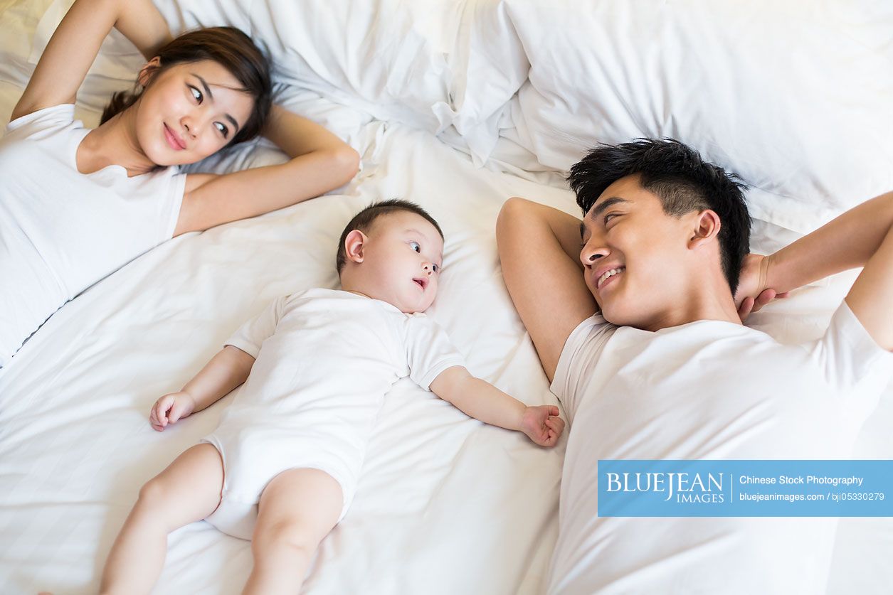 Happy young Chinese family lying on bed-High-res stock photo for download