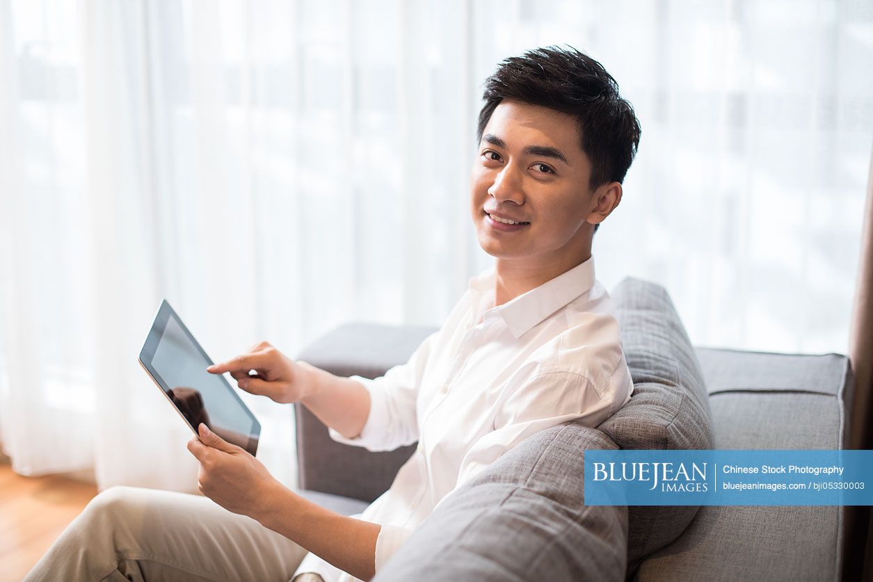 Cheerful young Chinese man using digital tablet at home-High-res stock ...