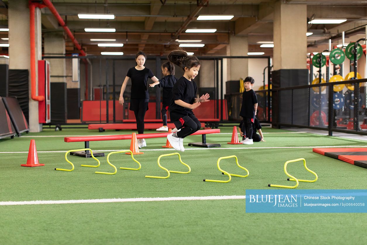 Active Chinese children having exercise class with their coach in gym ...