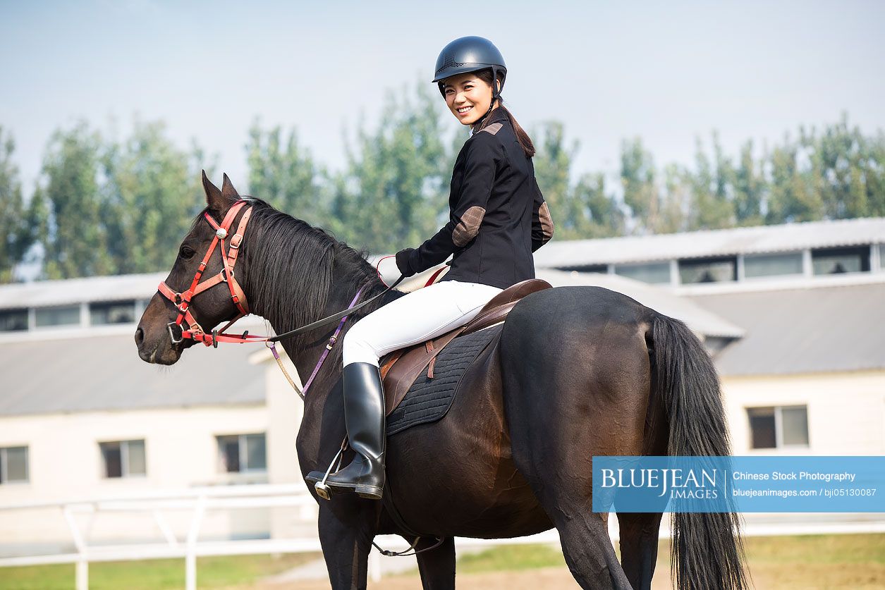 Cheerful young Chinese woman riding horse-High-res stock photo for download