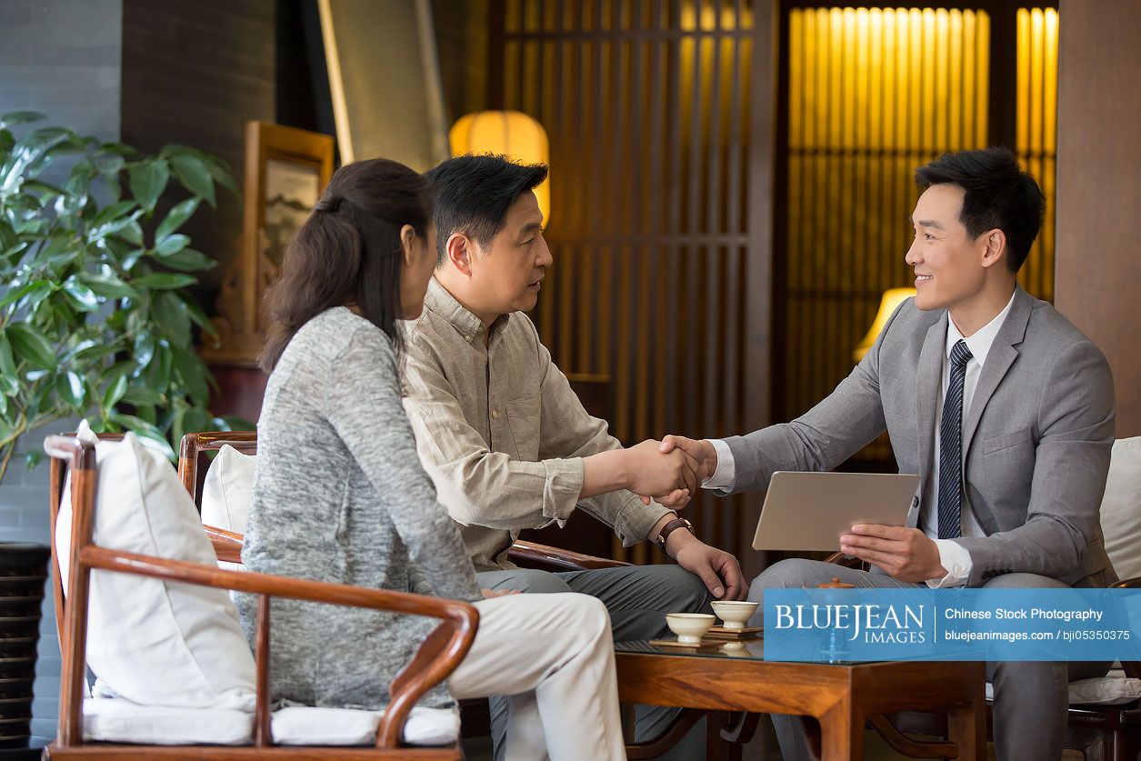 Confident Chinese financial consultant shaking hands with mature couple ...
