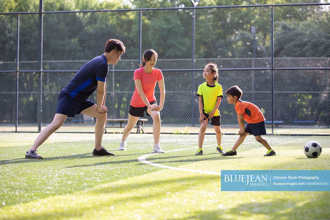 Happy young Chinese family warming up on soccer field-High-res stock photo for download