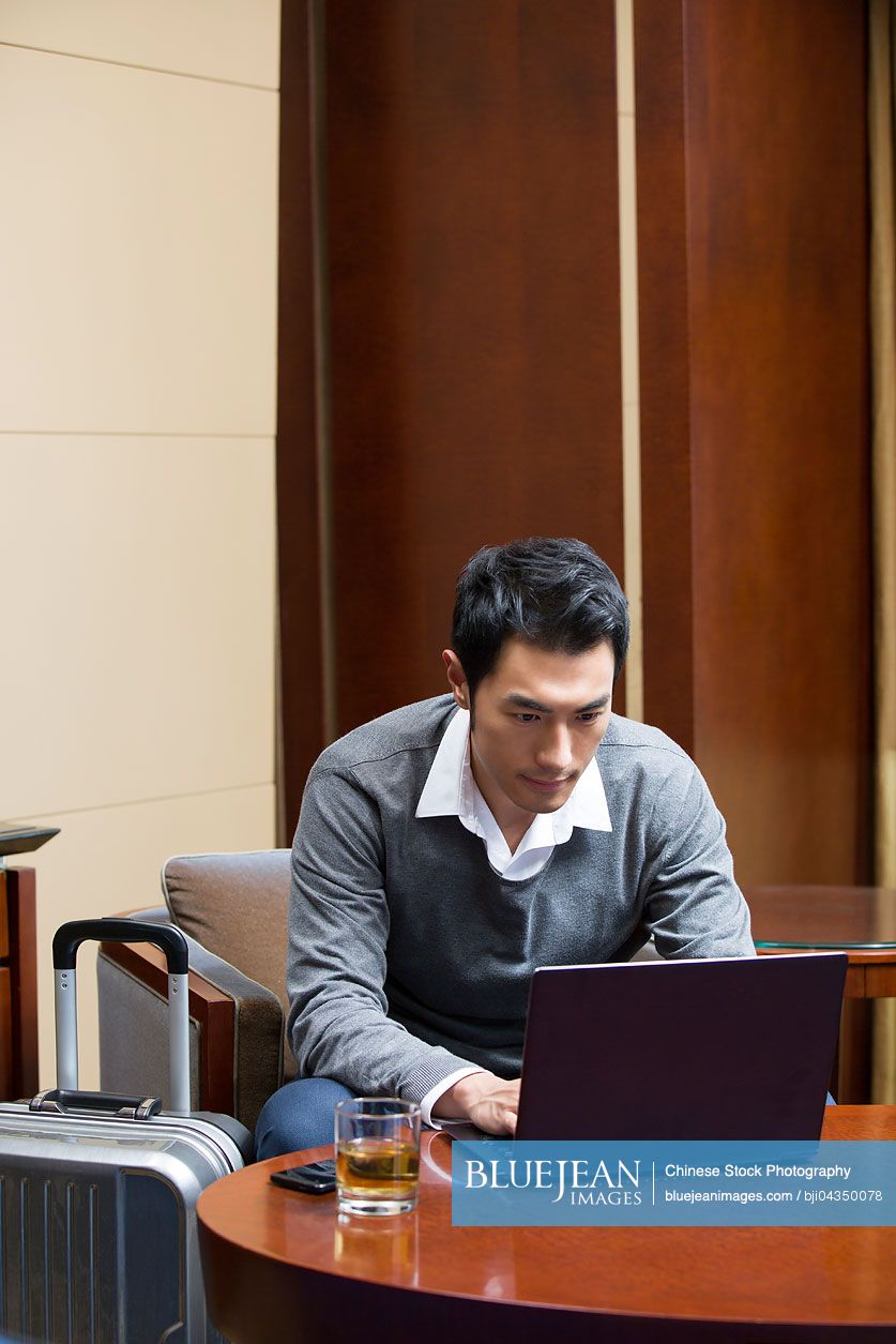 Young Chinese businessman using laptop in hotel room-High-res stock photo for download