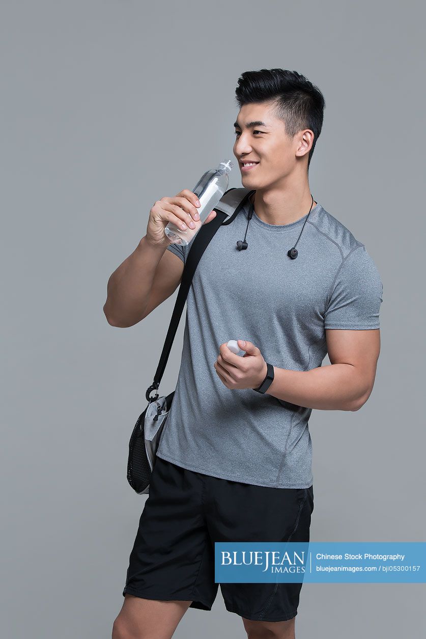 Cheerful young Chinese male athlete drinking a bottle of water-High-res stock photo for download