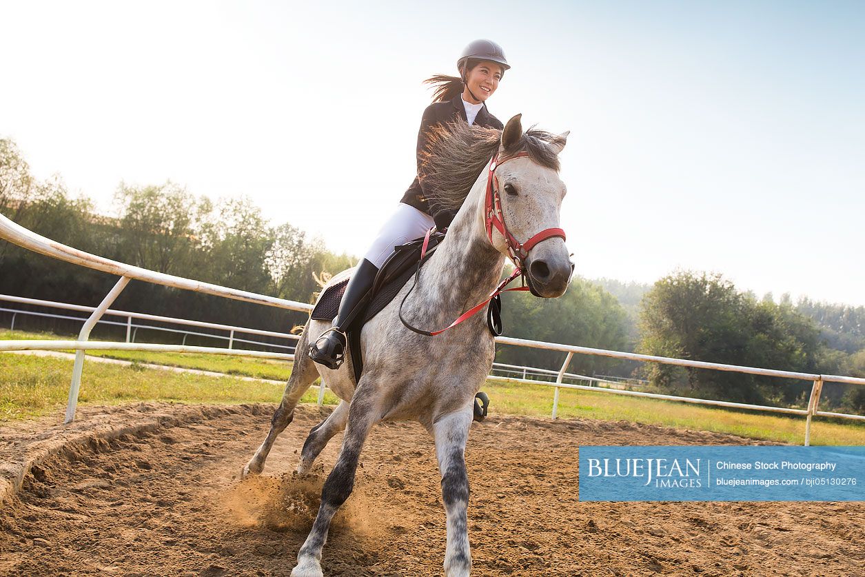 Cheerful young Chinese woman riding horse-High-res stock photo for download