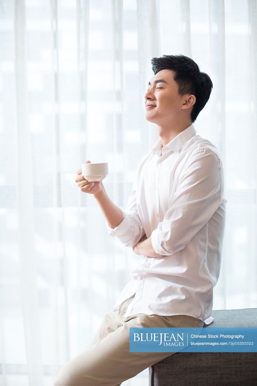 Cheerful young Chinese man drinking coffee at home-High-res stock photo ...