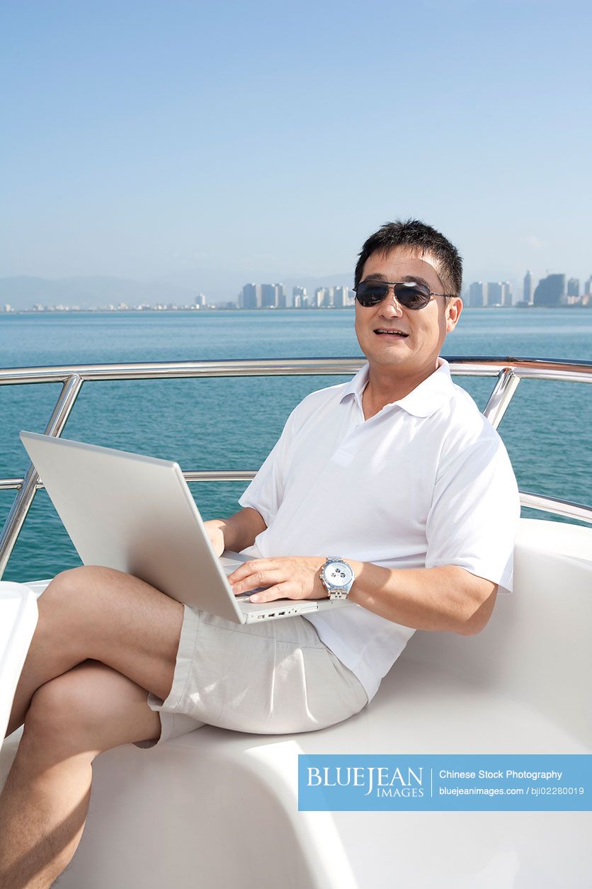 Chinese man using laptop on yacht-High-res stock photo for download