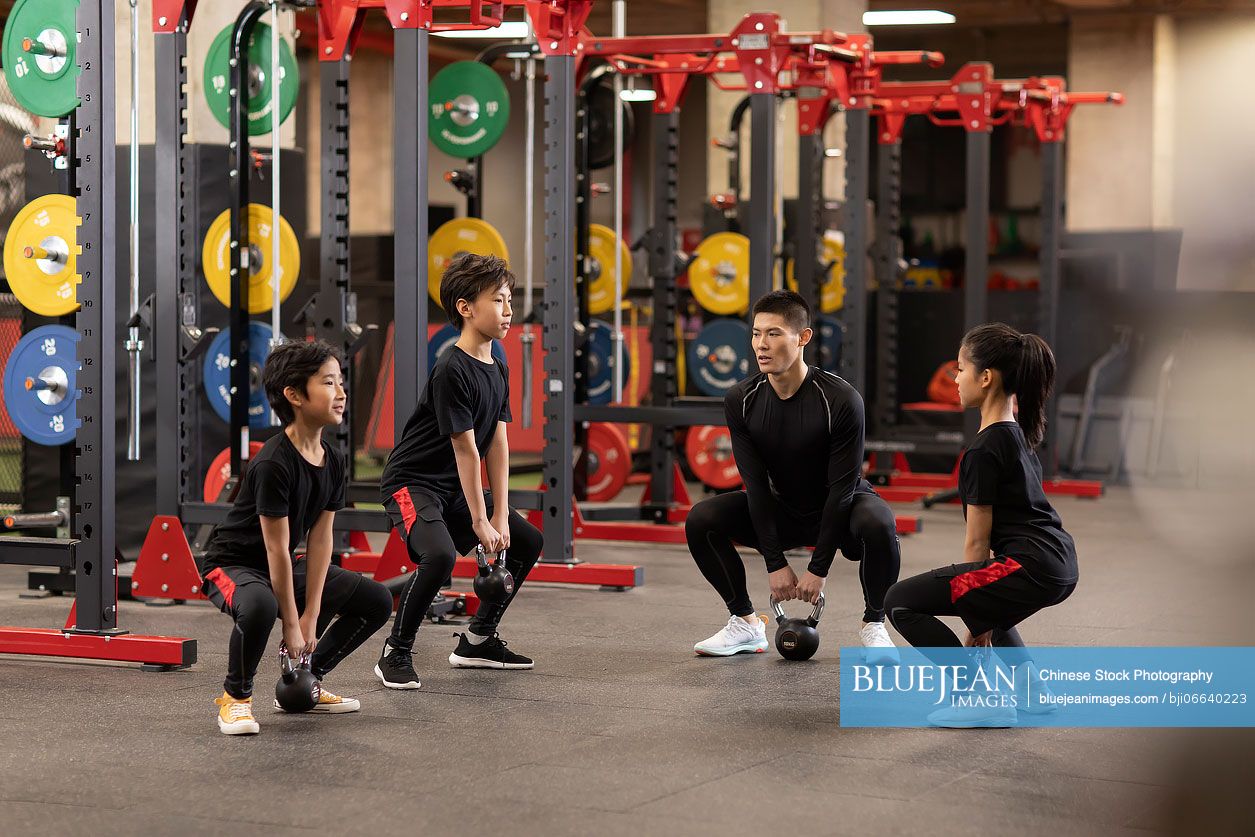Active Chinese children having exercise class with their coach in gym ...