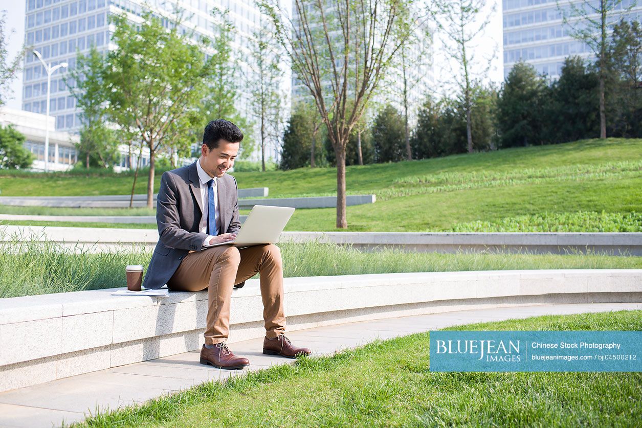 Chinese businessman using laptop outdoors-High-res stock photo for download