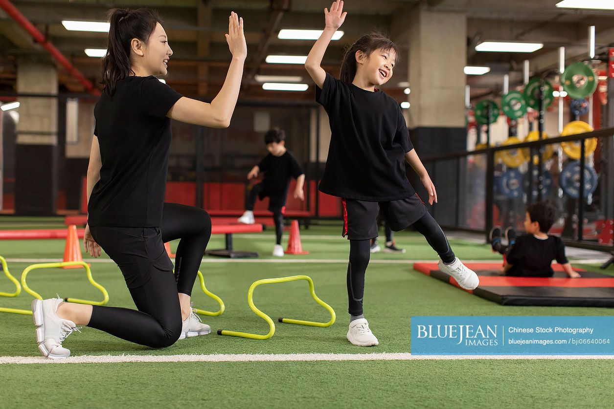 Active Chinese children having exercise class with their coach in gym ...