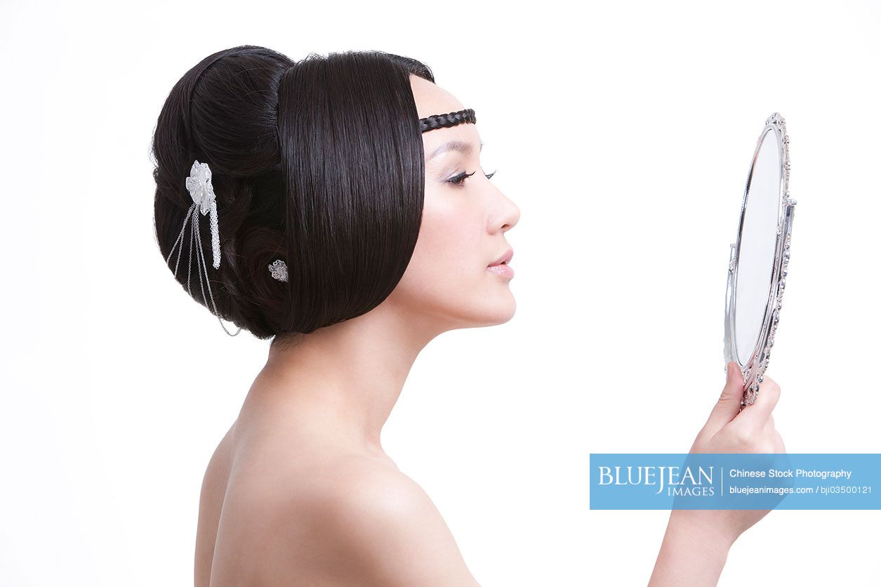 Young beautiful Chinese woman looking in handheld mirror-High-res stock photo for download