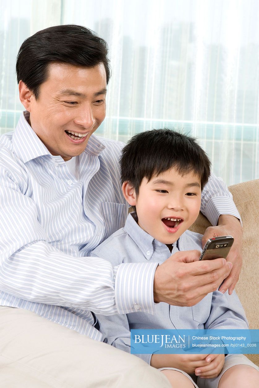 Chinese father and son using cell phone or PDA on sofa-High-res stock ...