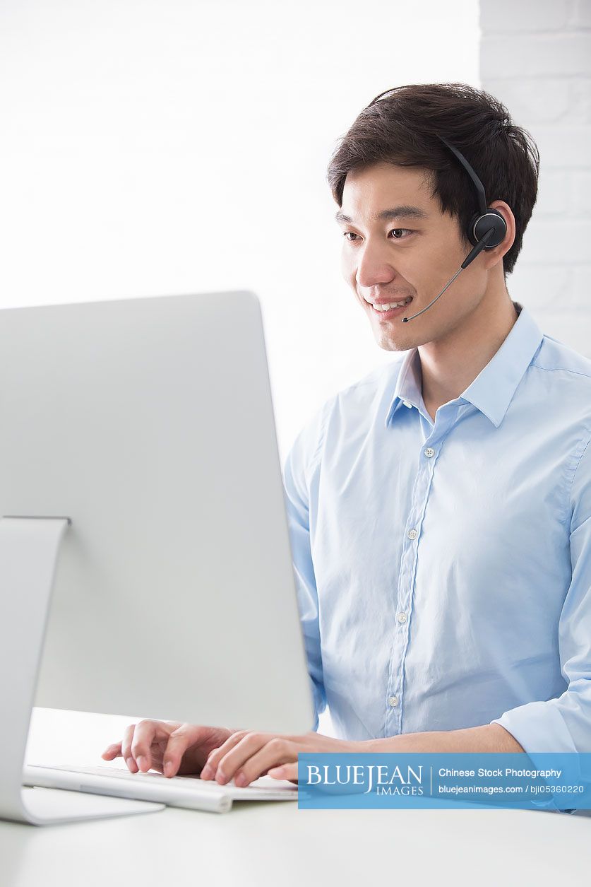 Cheerful young Chinese businessman with headset in office-High-res stock photo for download