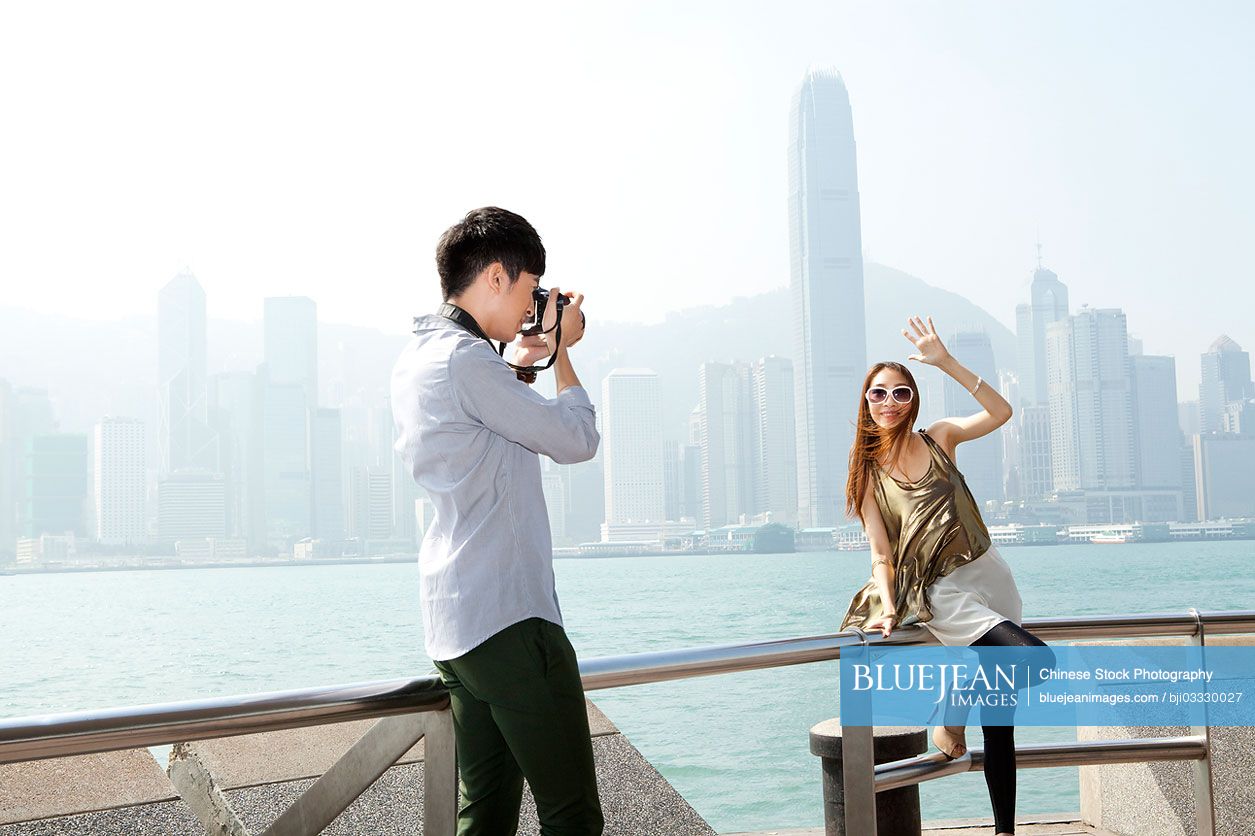 Happy young Chinese man photographing young women with SLR camera in ...