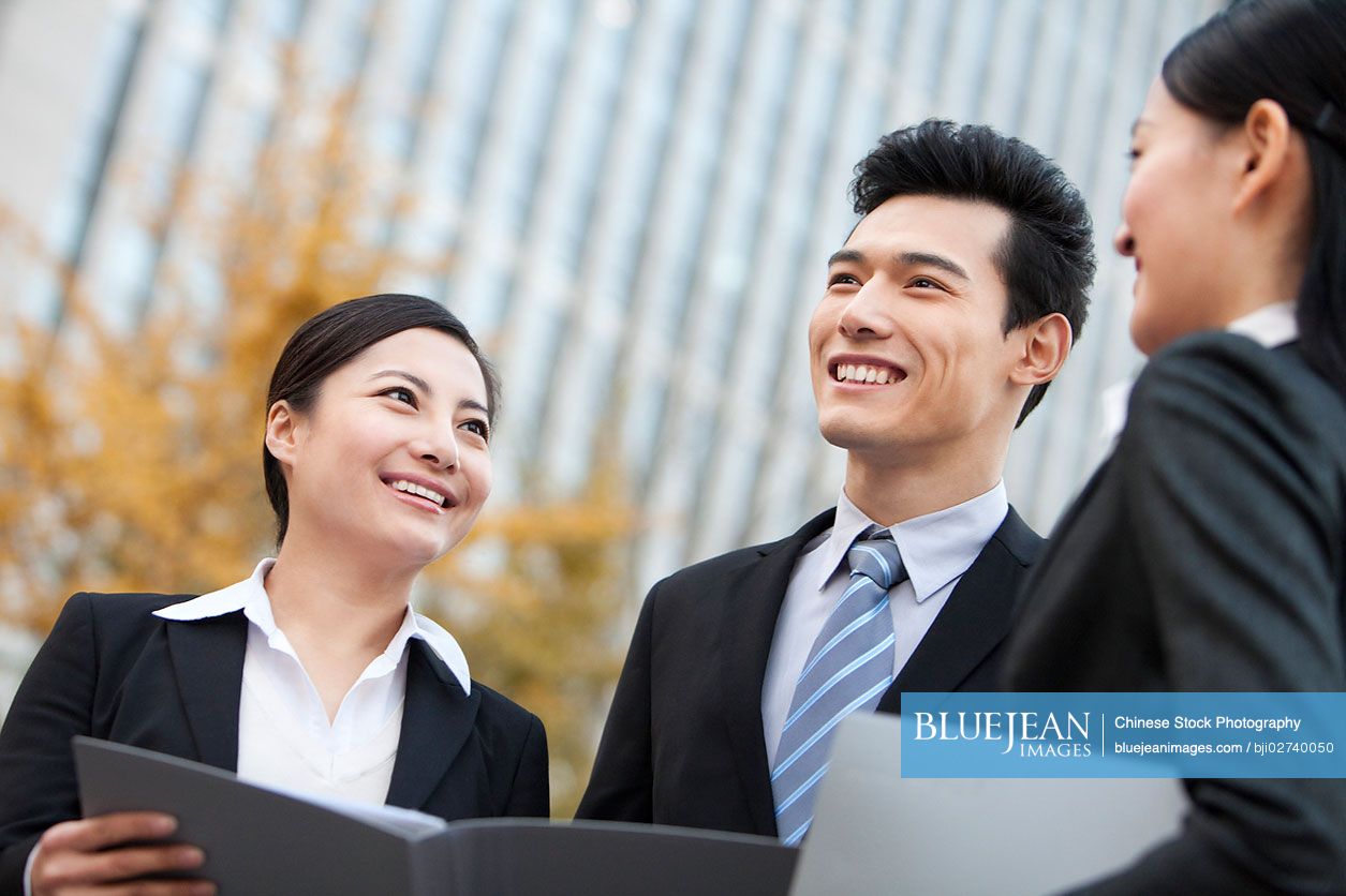 A team of Chinese businesspeople outside office buildings looking at a ...