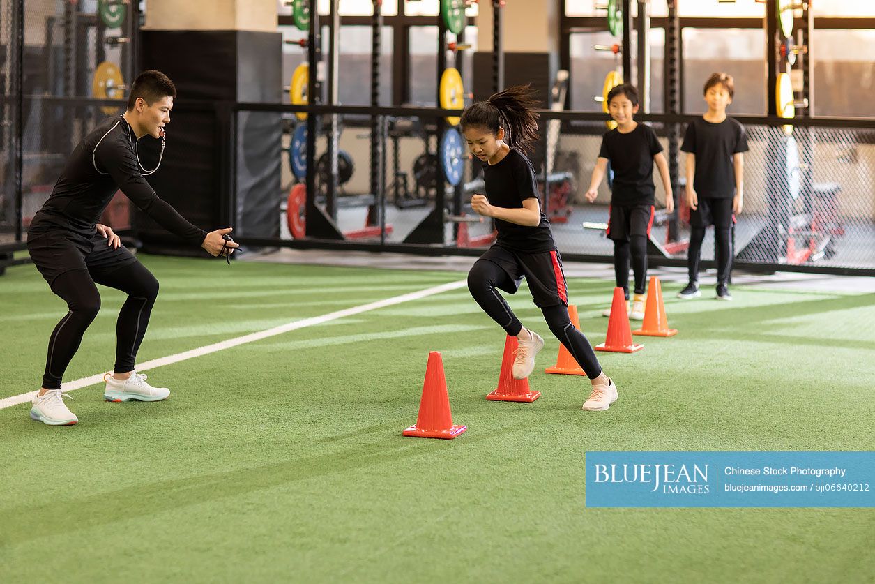 Active Chinese children having exercise class with their coach in gym ...