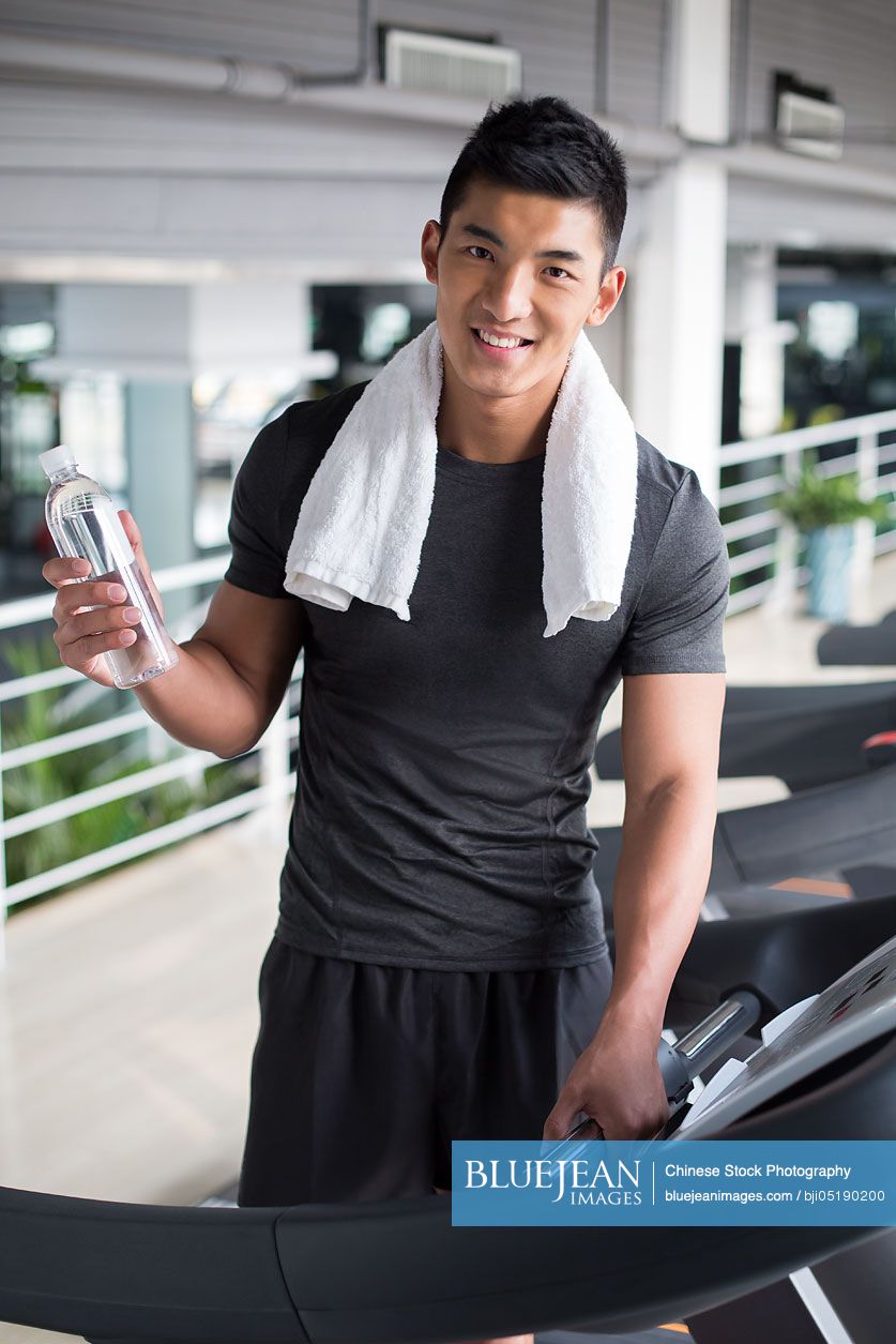 Young Chinese man holding a bottle of water on a treadmill-High-res stock photo for download