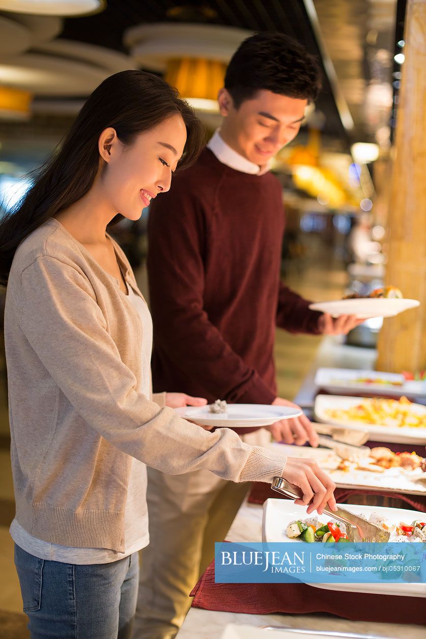 Cheerful young Chinese couple taking food from buffet table-High-res ...