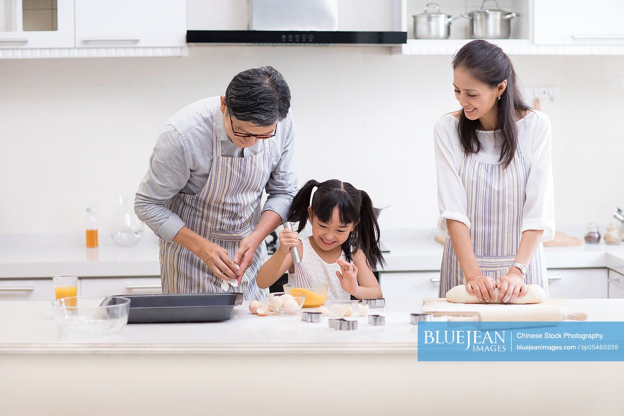 Happy little Chinese girl and grandparents baking cookies in kitchen ...