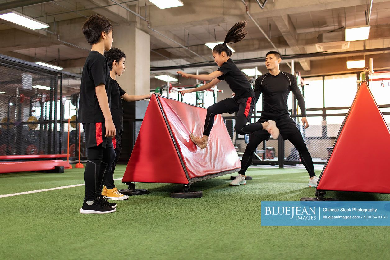 Active Chinese children having exercise class with their coach in gym ...