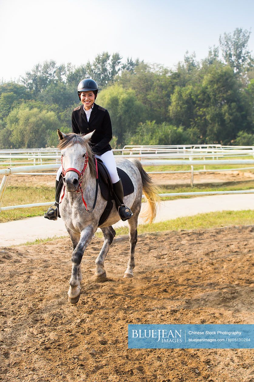 Cheerful young Chinese woman riding horse-High-res stock photo for download