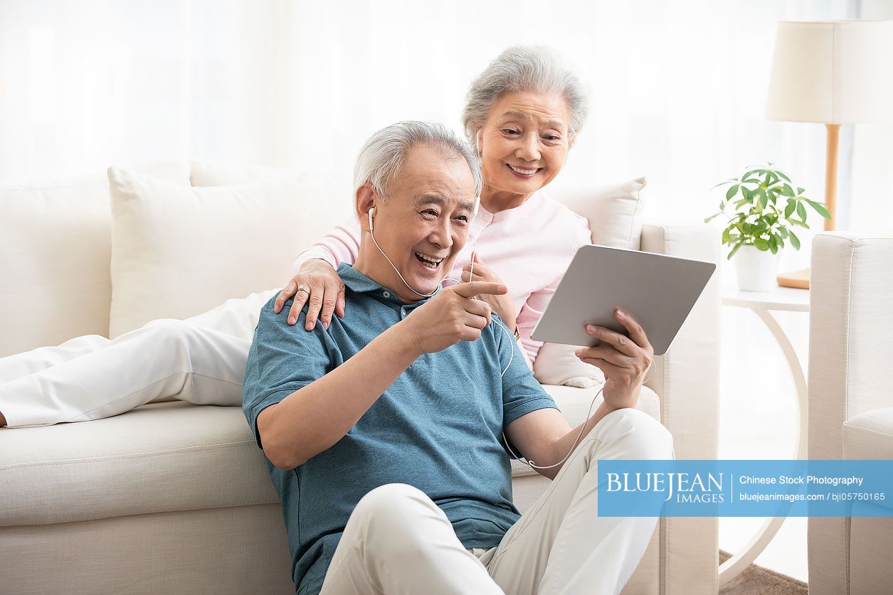 Happy senior Chinese couple using digital tablet in living room-High-res stock photo for download