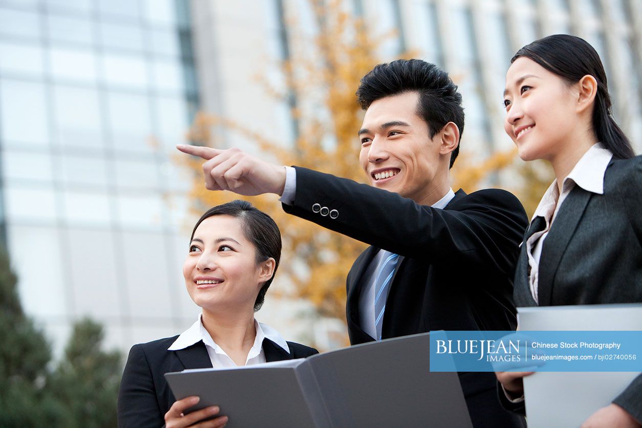 A team of Chinese businesspeople outside office buildings pointing and ...