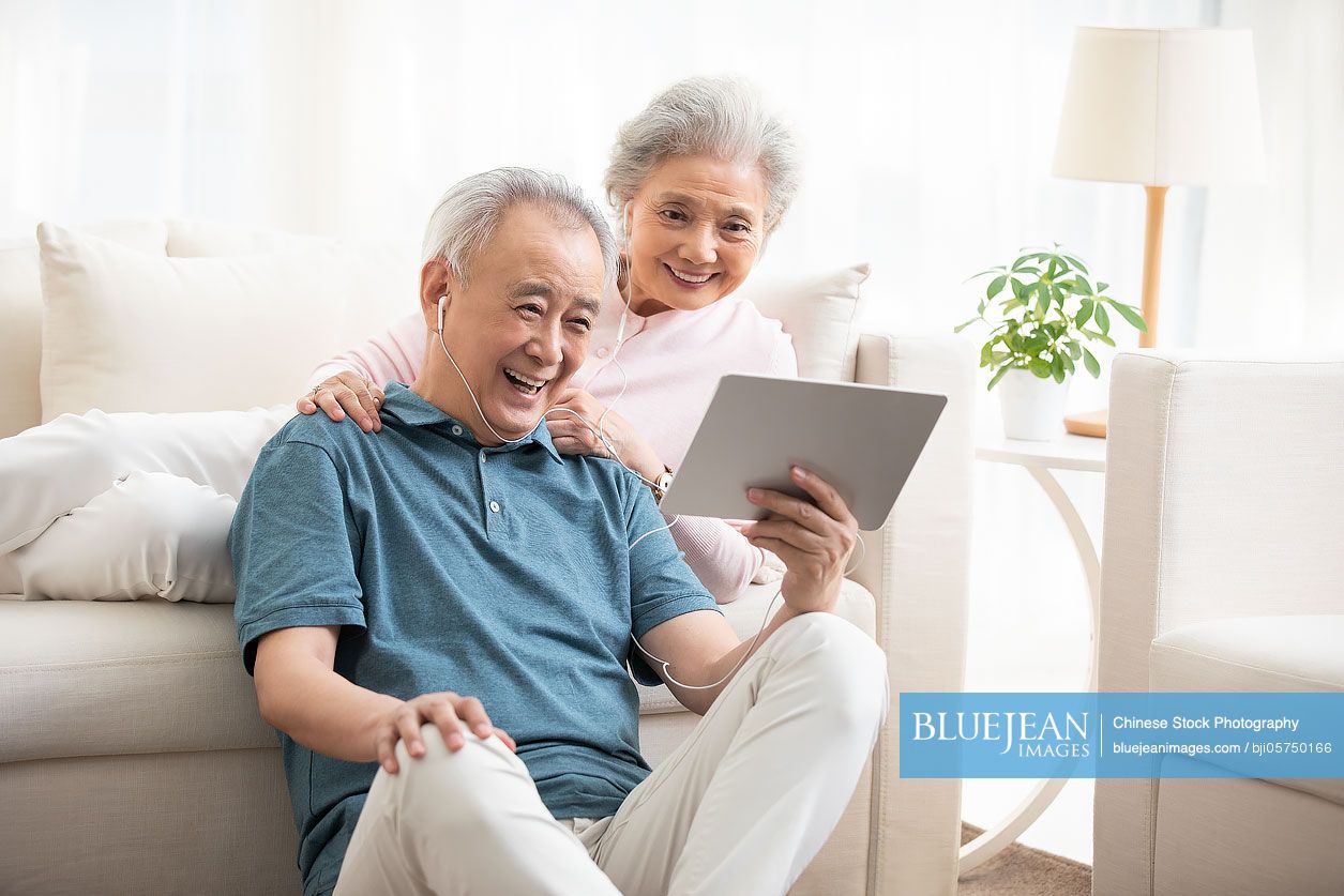 Happy senior Chinese couple using digital tablet in living room-High-res stock photo for download