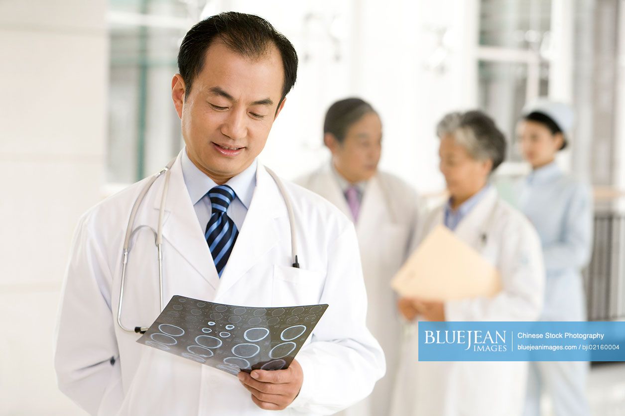 Chinese doctor looking at CAT scan with doctors and nurse in background-High-res stock photo for ...