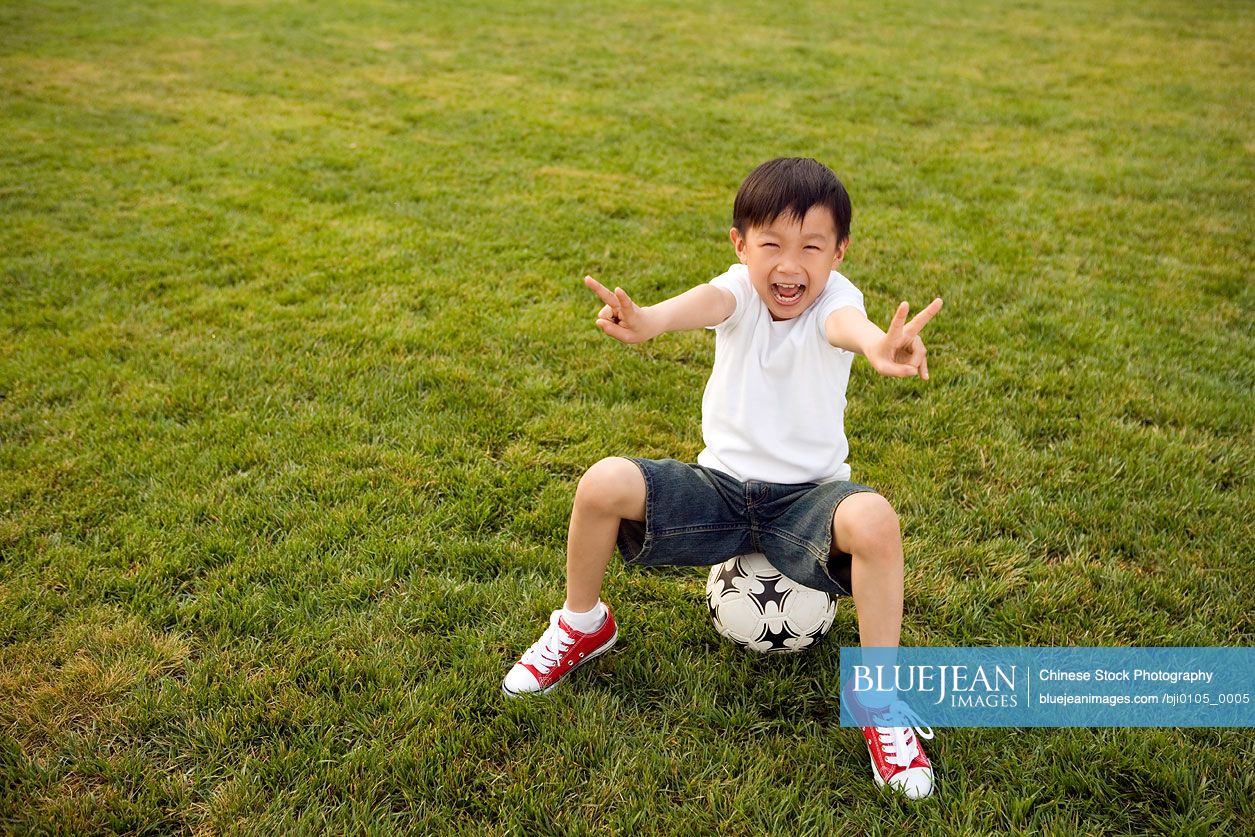 Chinese Boy Sitting On Soccer, Giving Victory Sign-High-res stock photo for download