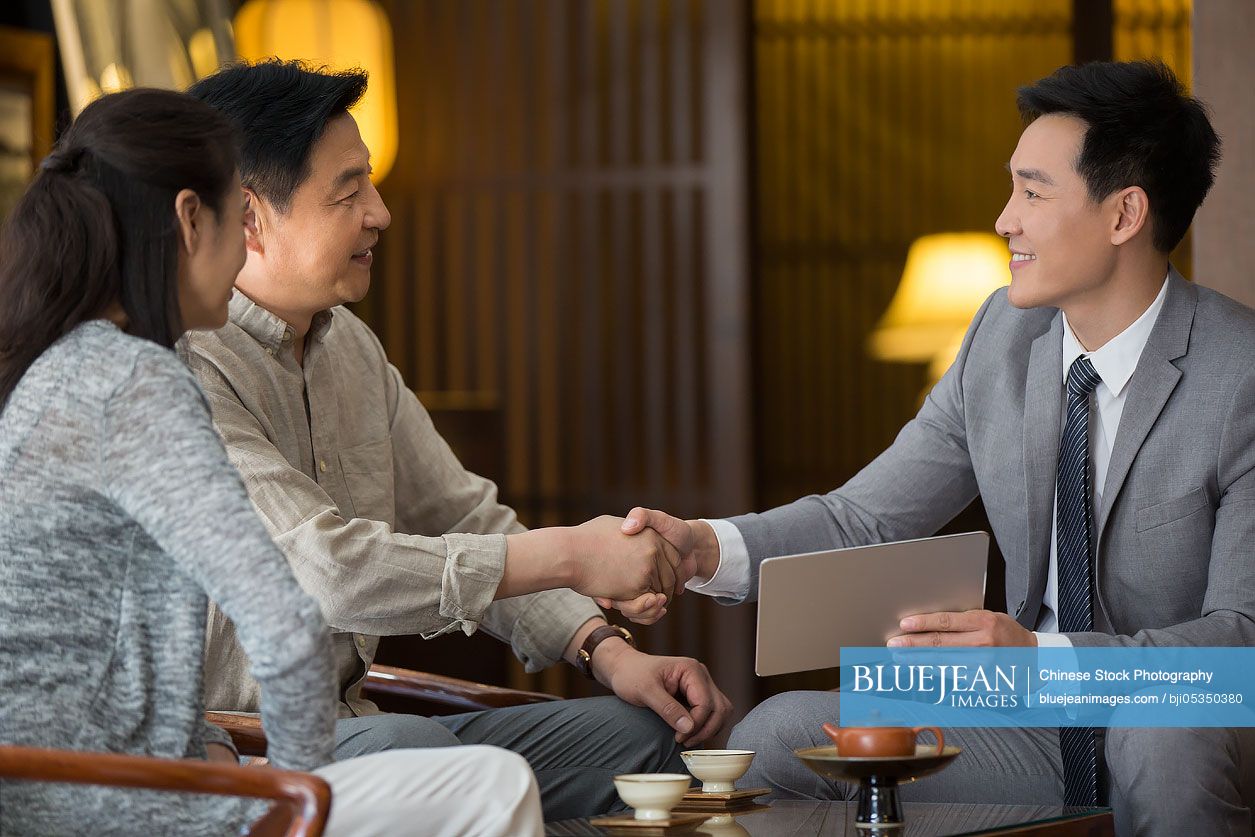 Confident Chinese financial consultant shaking hands with mature couple ...