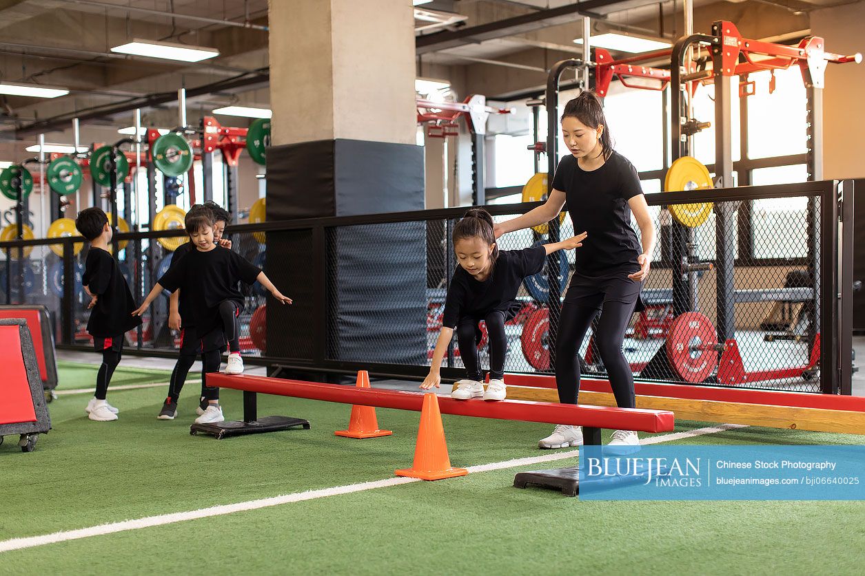 Active Chinese children having exercise class with their coach in gym ...