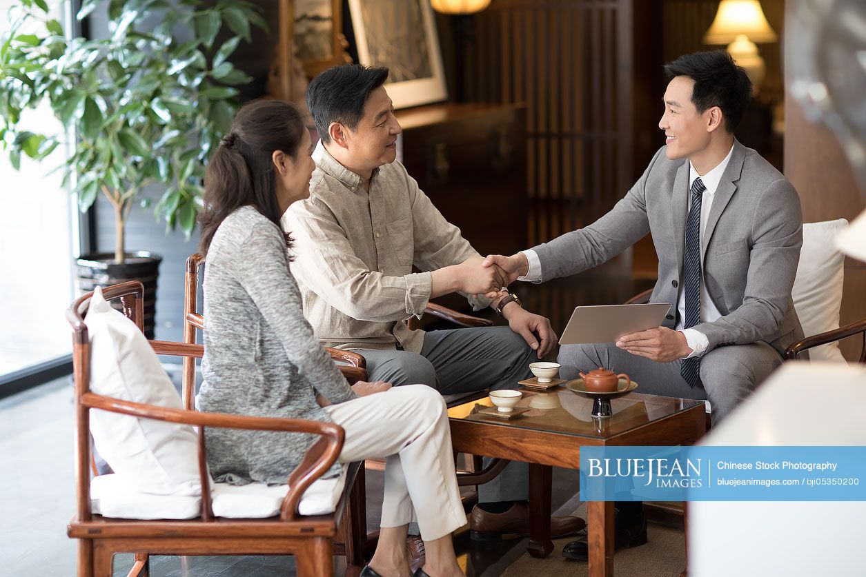 Confident Chinese financial consultant shaking hands with mature couple ...
