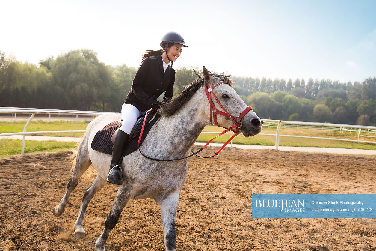Cheerful young Chinese woman riding horse-High-res stock photo for download