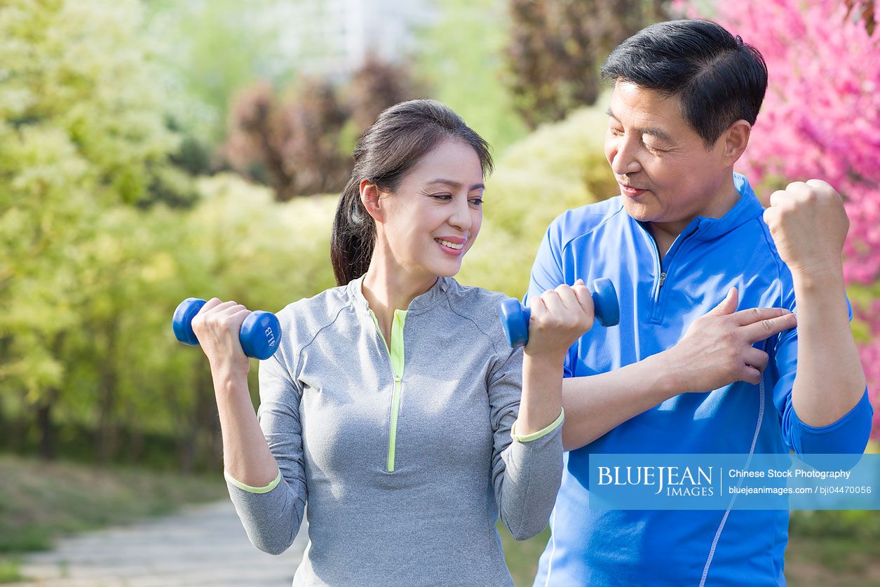 Happy mature Chinese couple exercising with dumbbell in park-High-res stock photo for download