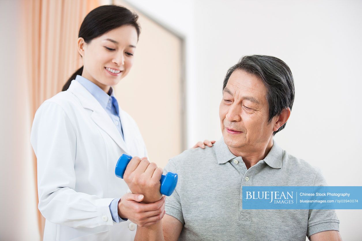 Senior Chinese patient exercising with dumbbell under doctor's help ...